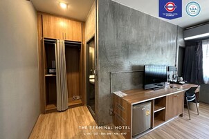 Quarto de hotel com guarda-roupa de madeira, uma kitchenette pequena, televisão e secretária.