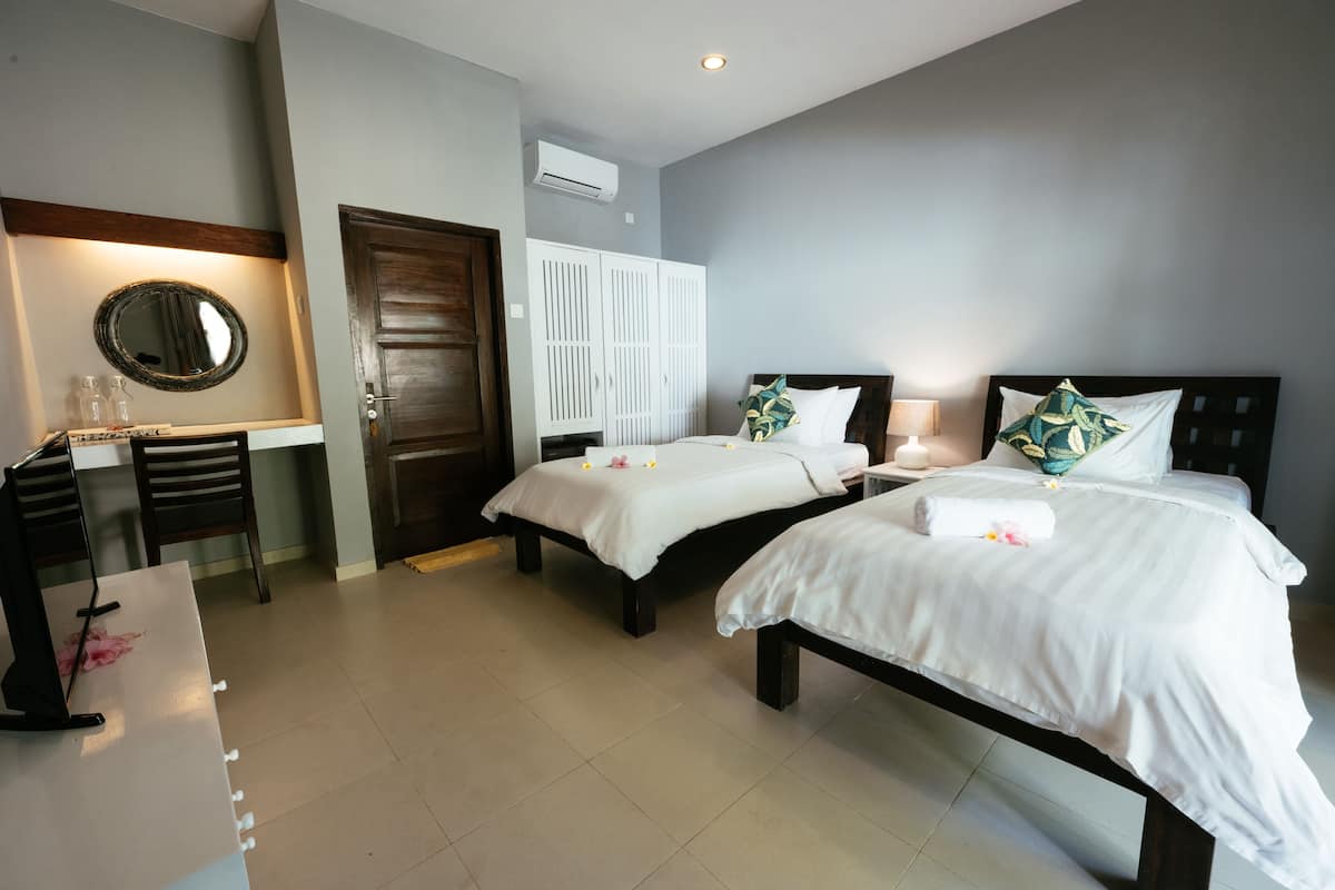 Quarto de hotel com duas camas, uma escrivaninha, um espelho e um guarda-roupa.