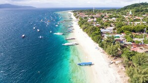 Vista aérea de uma área costeira com praia, barcos e uma região densamente povoada com edifícios.