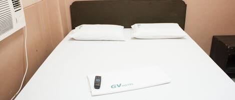 Uma cama de solteiro com lençóis brancos e um controle remoto, identificado como
