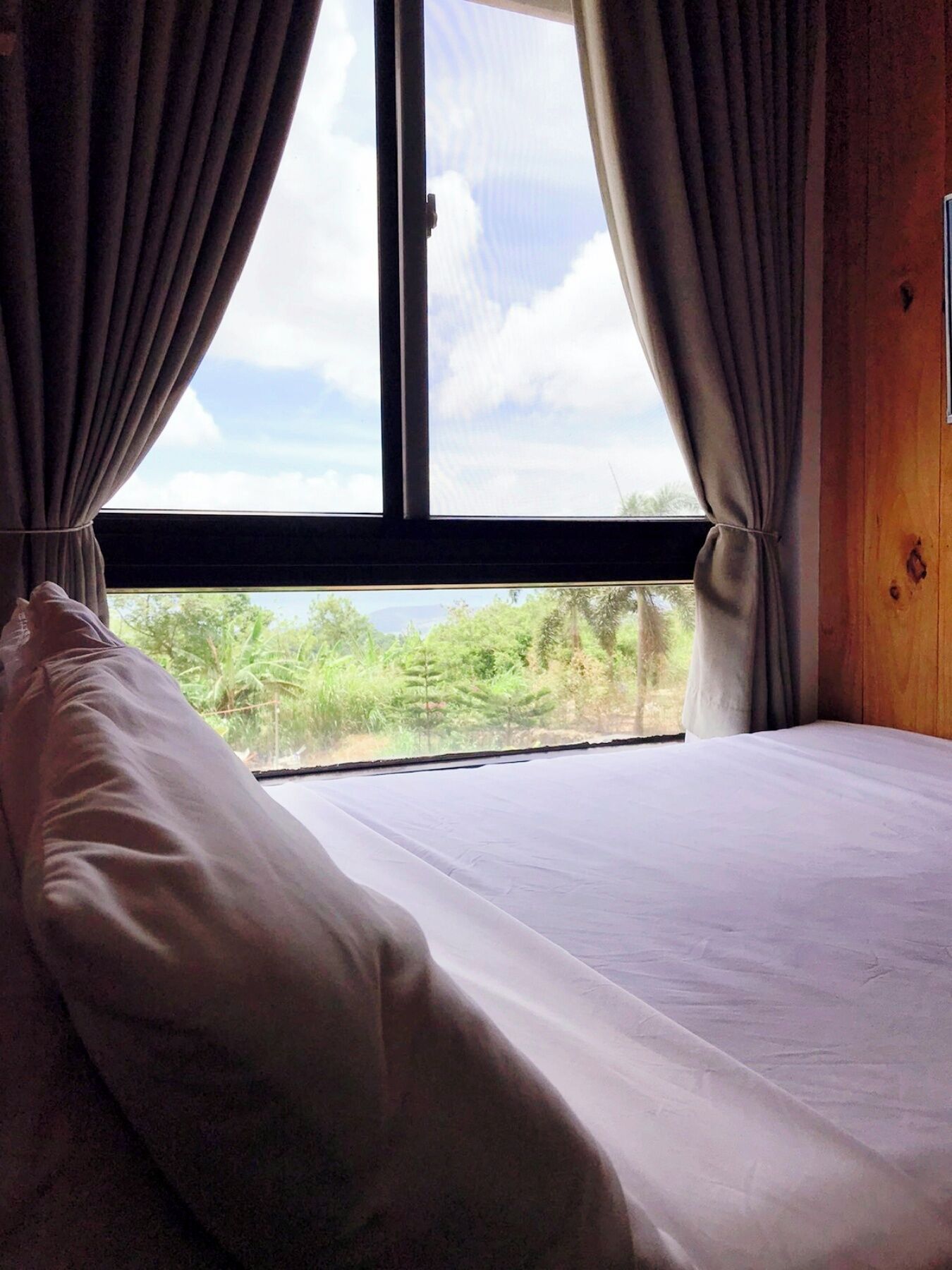 Cama com vista para uma paisagem tropical através de uma janela com cortinas.