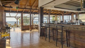 Uma área de refeições ao ar livre ampla, com vigas de madeira e vista para o mar.