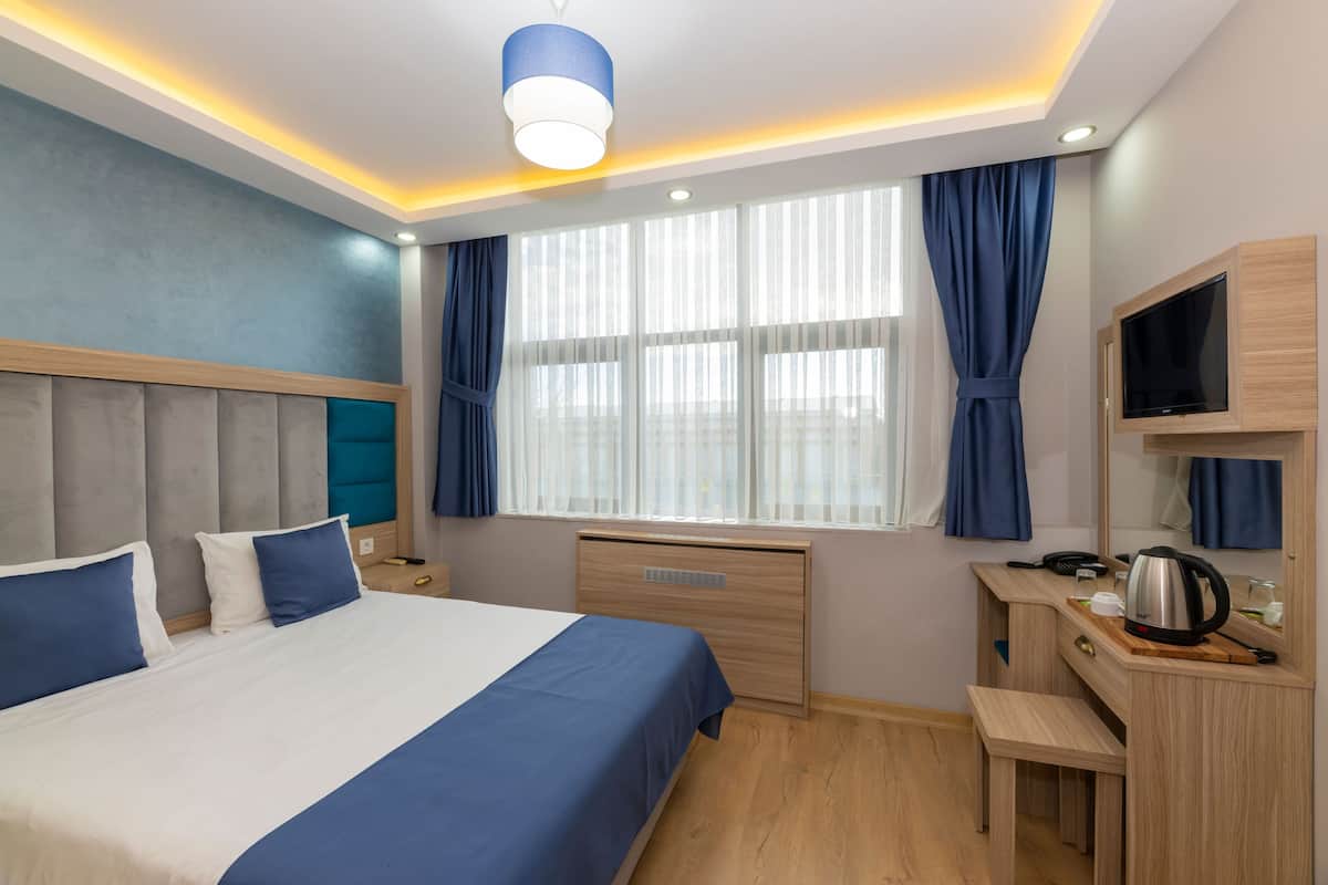 Quarto de hotel moderno com uma cama grande, uma escrivaninha, uma televisão e uma janela com cortinas.