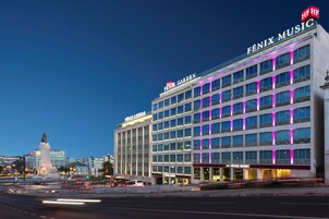 Um hotel com vários andares, um destaque para o letreiro 'FENIX MUSIC' e uma estátua ao fundo.