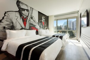 Quarto de hotel com duas camas, ampla vista para a cidade e um mural na parede.