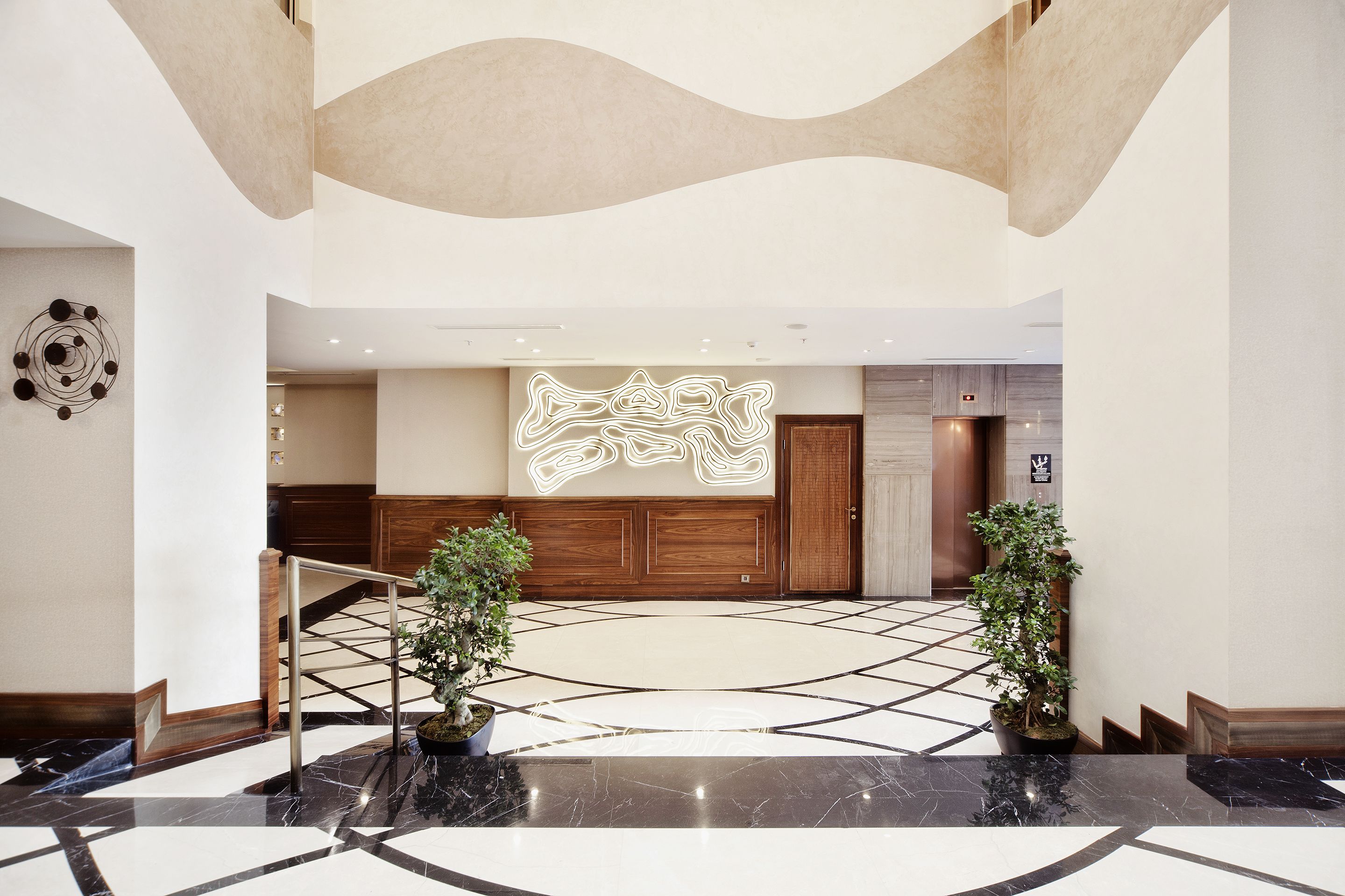 Um hall amplo com piso de mármore, painéis de madeira e duas plantas em vasos.
