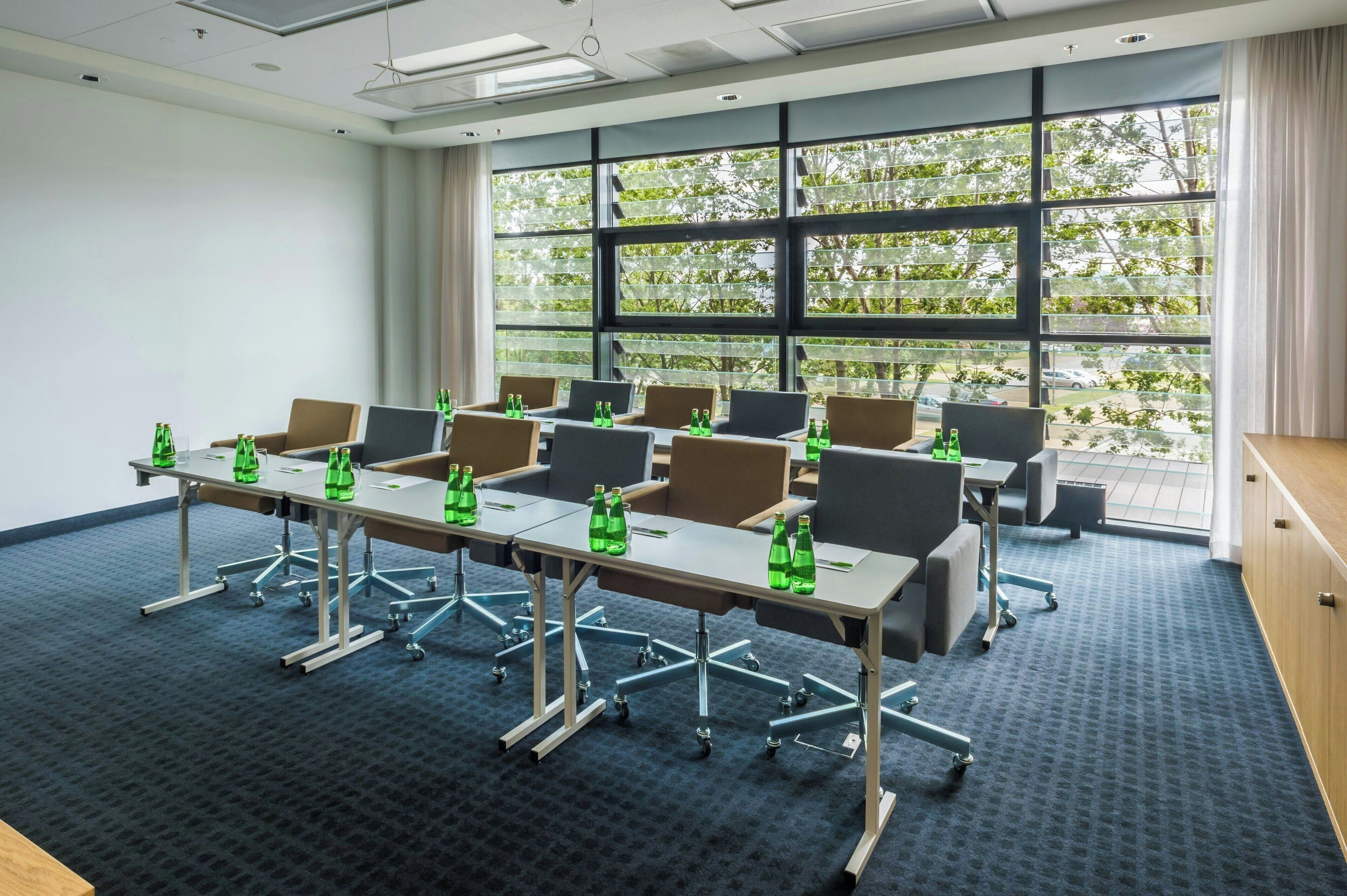 Uma sala de conferência com uma mesa comprida, cadeiras e garrafas verdes.