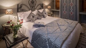 Quarto com cama grande, teto decorativo e mesa de cabeceira com luminária e flores.