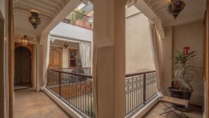 Um corredor com varanda, portas ornamentadas e um vaso com planta.