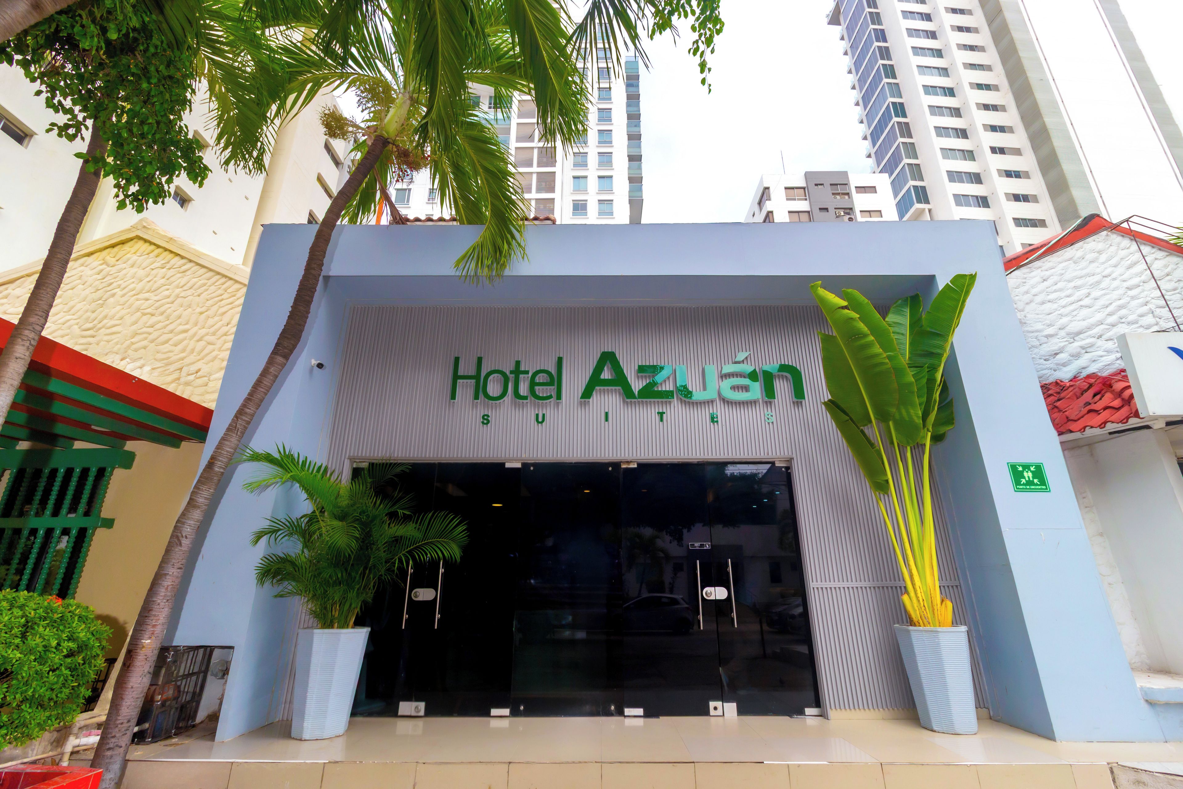 Entrada do Hotel Azuan, com fachada moderna, grandes vasos de plantas e vista clara dos edifícios ao redor.