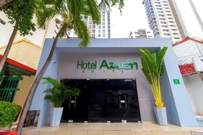 Entrada do Hotel Azuan, com fachada moderna, grandes vasos de plantas e vista clara dos edifícios ao redor.