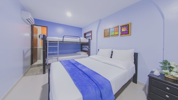 Quarto com beliches, mesa de cabeceira com telefone e cesto, e duas obras de arte coloridas nas paredes.