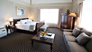 Quarto de hotel com cama, sofá, mesa de centro com frutas, luminária e armário.