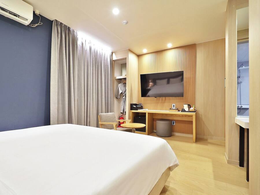 Quarto de hotel com cama, secretária, televisão e chuveiro.