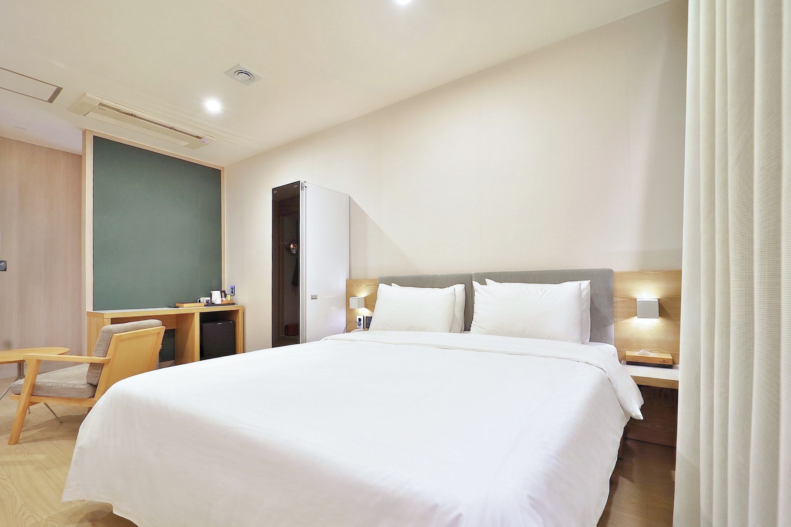 Quarto de hotel com uma cama grande, uma mesa de trabalho, um guarda-roupa e uma mesa de cabeceira com luminárias.