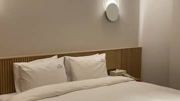 Quarto de hotel com cama bem arrumada, telefone de mesa e luminária fixada na parede.