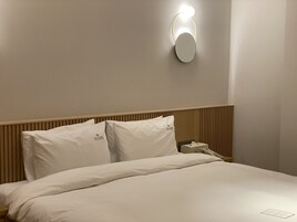 Quarto de hotel com cama bem arrumada, telefone de mesa e luminária fixada na parede.