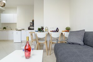 Uma cozinha moderna com armários brancos, uma mesa de jantar com cadeiras e um sofá cinza na sala de estar.