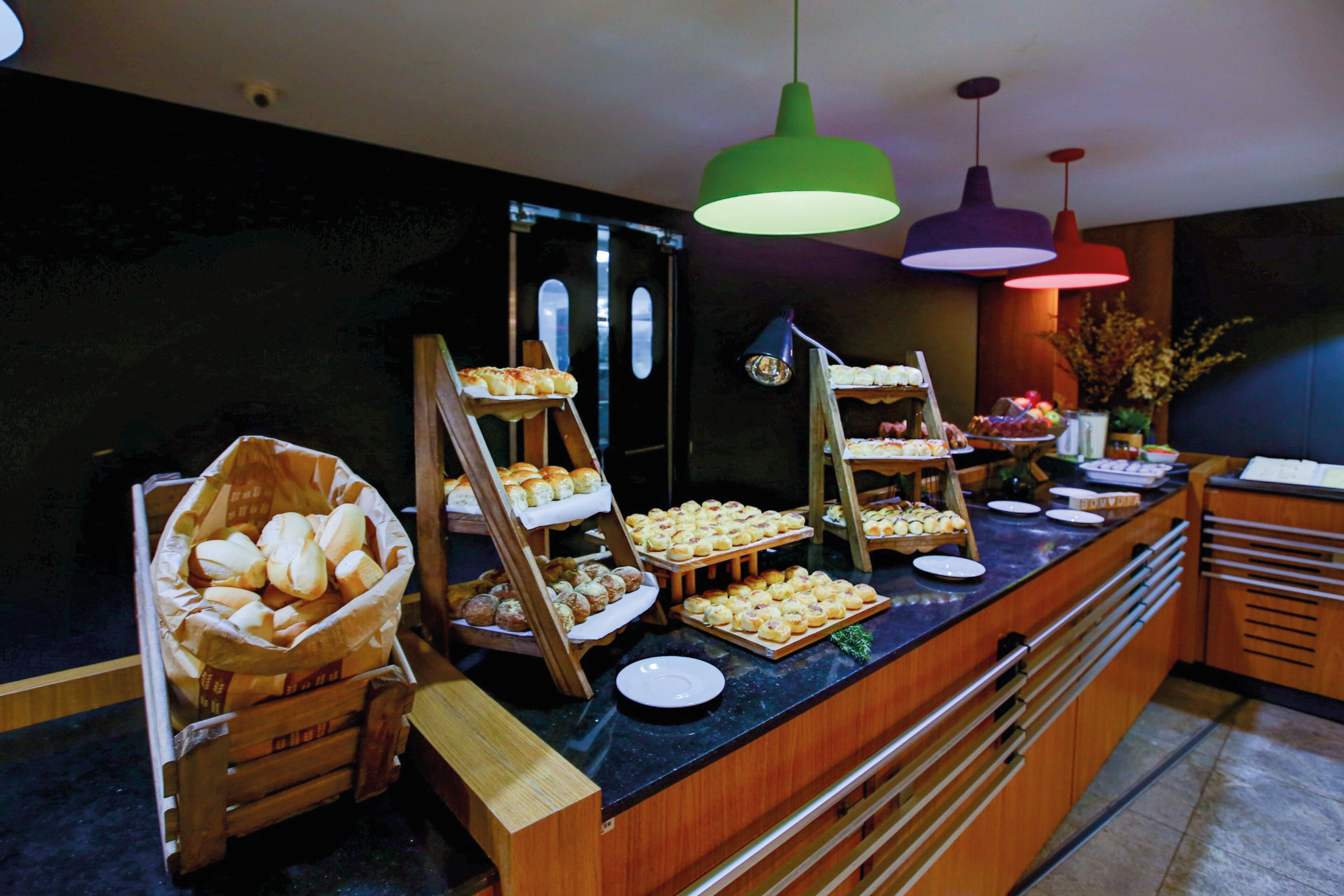 Disposição de buffet com diversos alimentos expostos em suportes de madeira e uma cesta grande de pão.