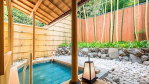 Um deck de madeira com hidromassagem, um candeeiro e uma cerca de bambu.