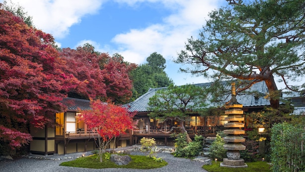 Um edifício japonês tradicional com fachada de madeira, um lança-pedras de pedra e um jardim bem cuidado com caminhos de cascalho e um pequeno lago.