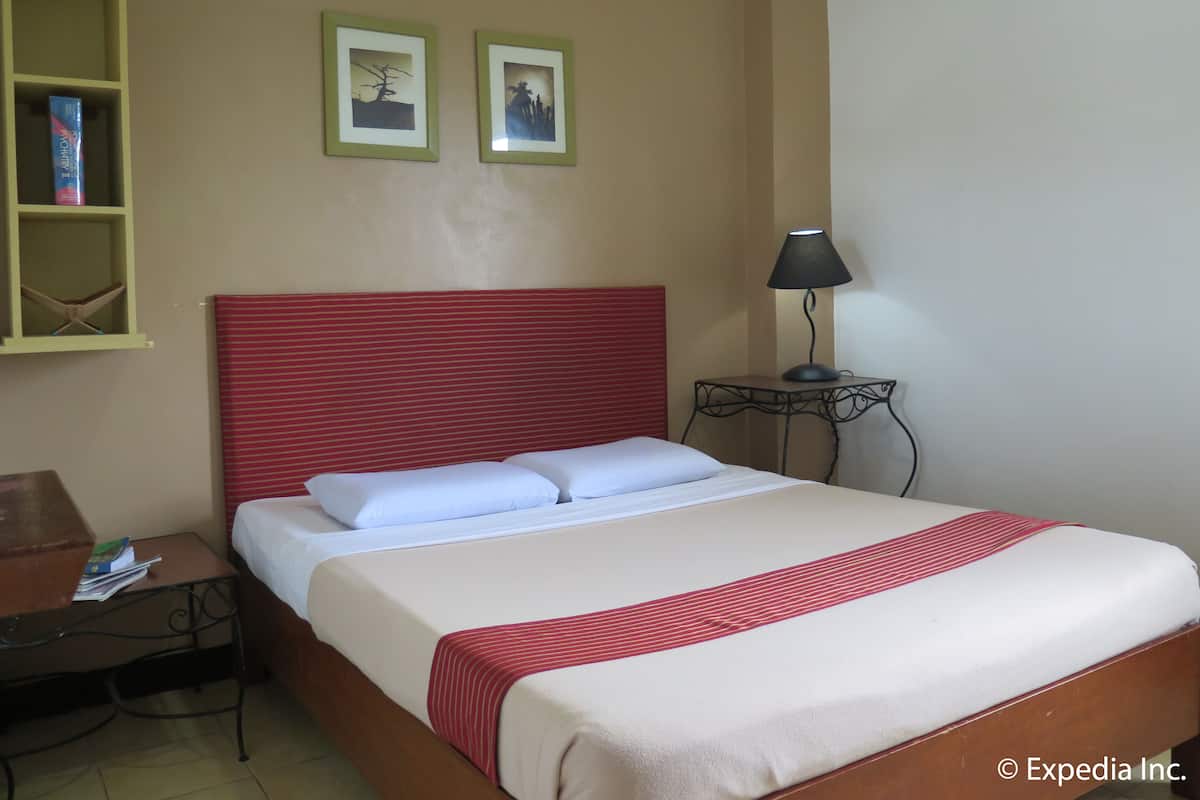 Quarto de hotel com uma cama, mesa de cabeceira, luminária e duas molduras na parede.