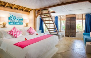 Quarto com cama, escada, uma cadeira azul e uma janela grande.