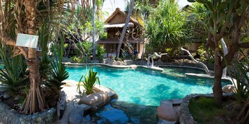 Piscina rodeada por vegetação tropical e uma estrutura com telhado de palha.