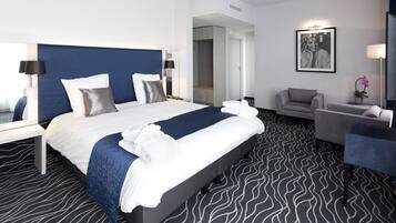 Quarto de hotel moderno com uma cama grande, área de estar e uma moldura na parede.