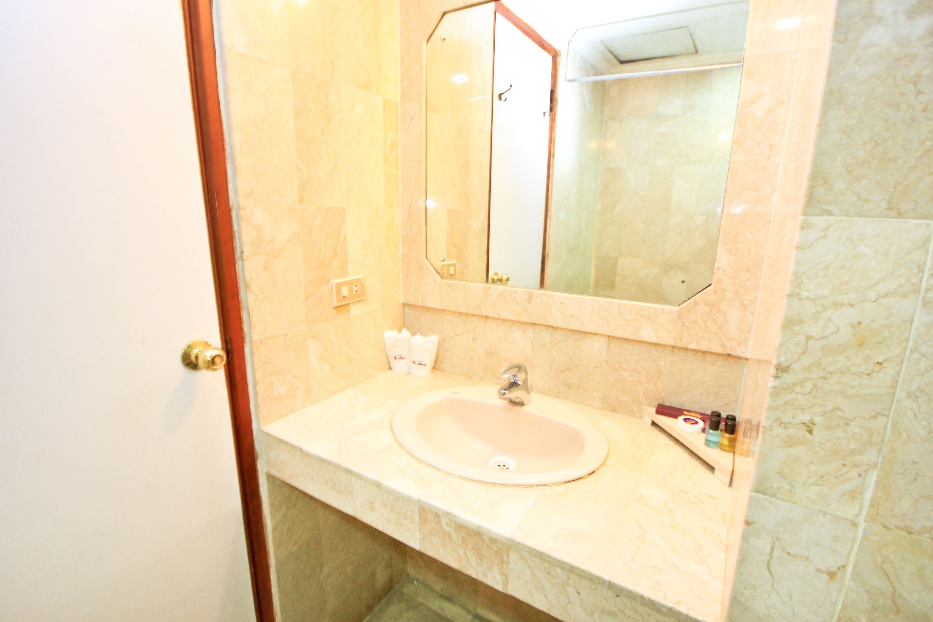 Casa de banho com lavatório de mármore, espelho e produtos de higiene na bancada.
