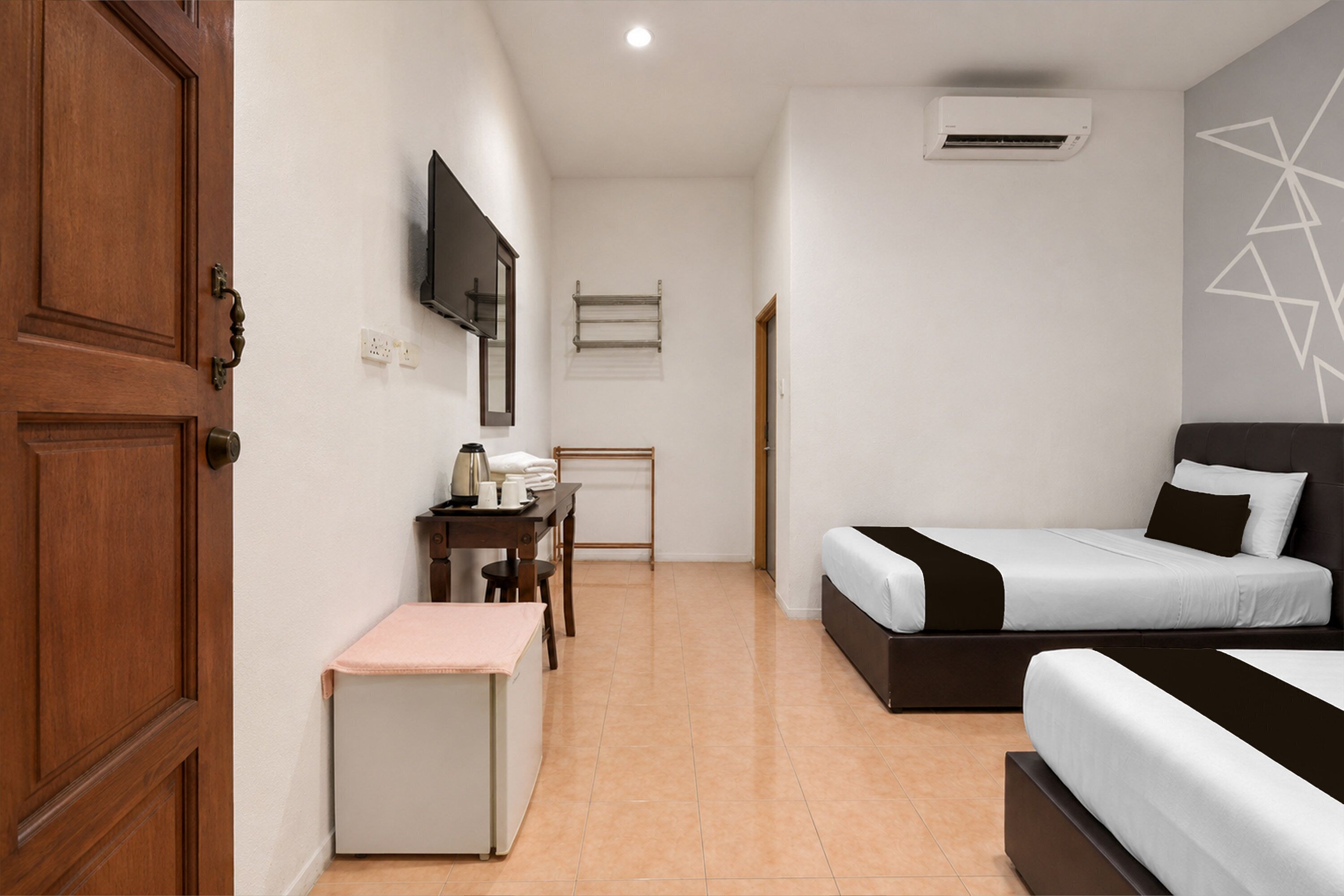 Quarto de hotel com porta de madeira, uma escrivaninha com cadeira, cama, televisão fixada na parede e unidade de ar condicionado.