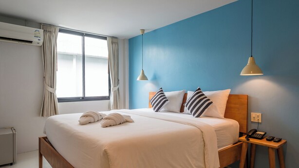 Quarto de hotel com cama, mesa de cabeceira com telefone e janela com cortinas.