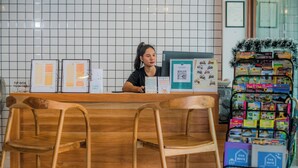 Bancada de recepção com parede revestida de azulejos, cadeiras de madeira e exposição de produtos Tiya House.