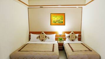 Quarto de hotel com duas camas de solteiro, mesa de cabeceira com abajur e quadro na parede.