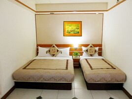Quarto de hotel com duas camas de solteiro, mesa de cabeceira com abajur e quadro na parede.