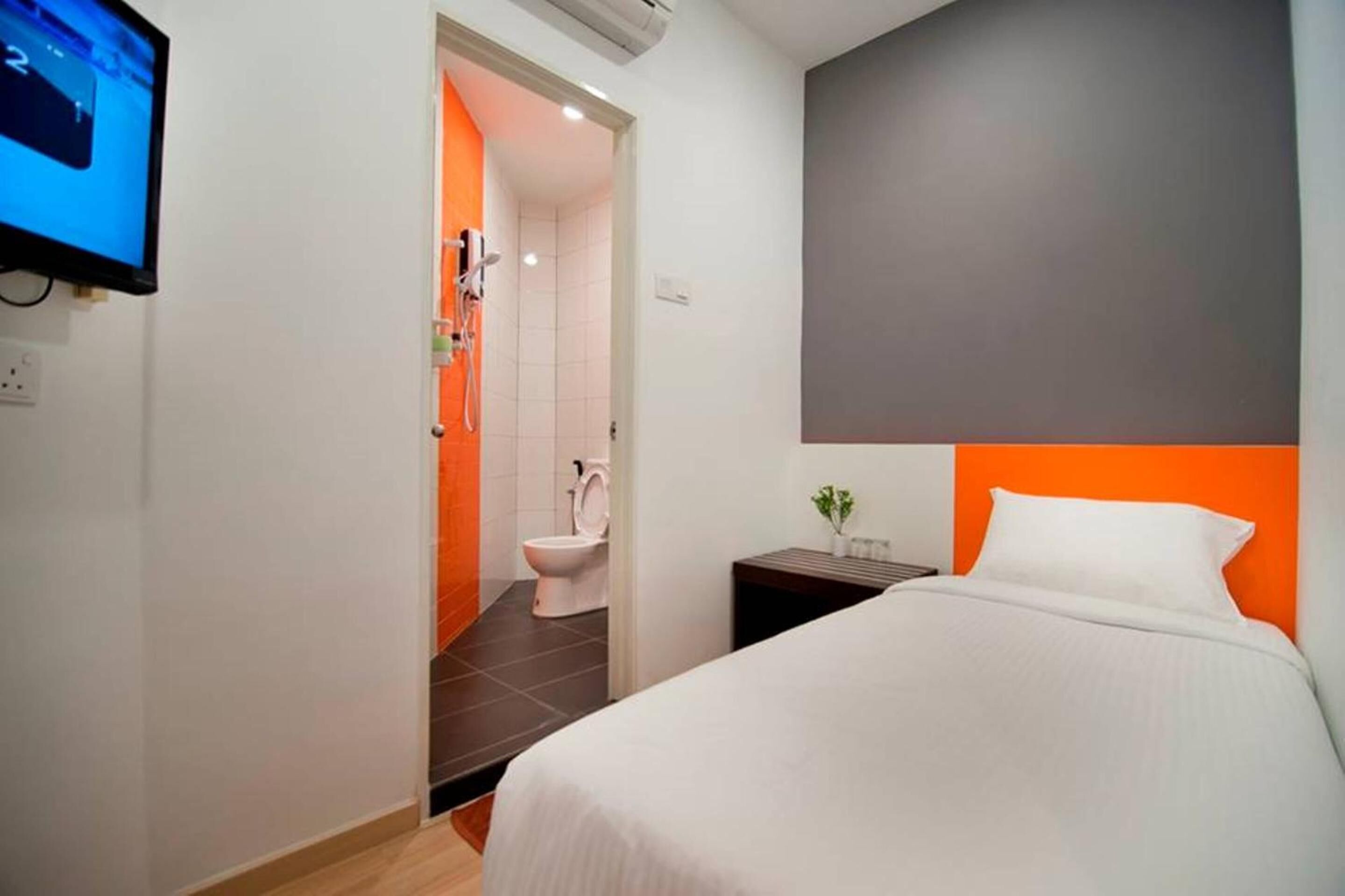Quarto de hotel com cama, mesa de cabeceira, televisão e parede com detalhes em laranja.