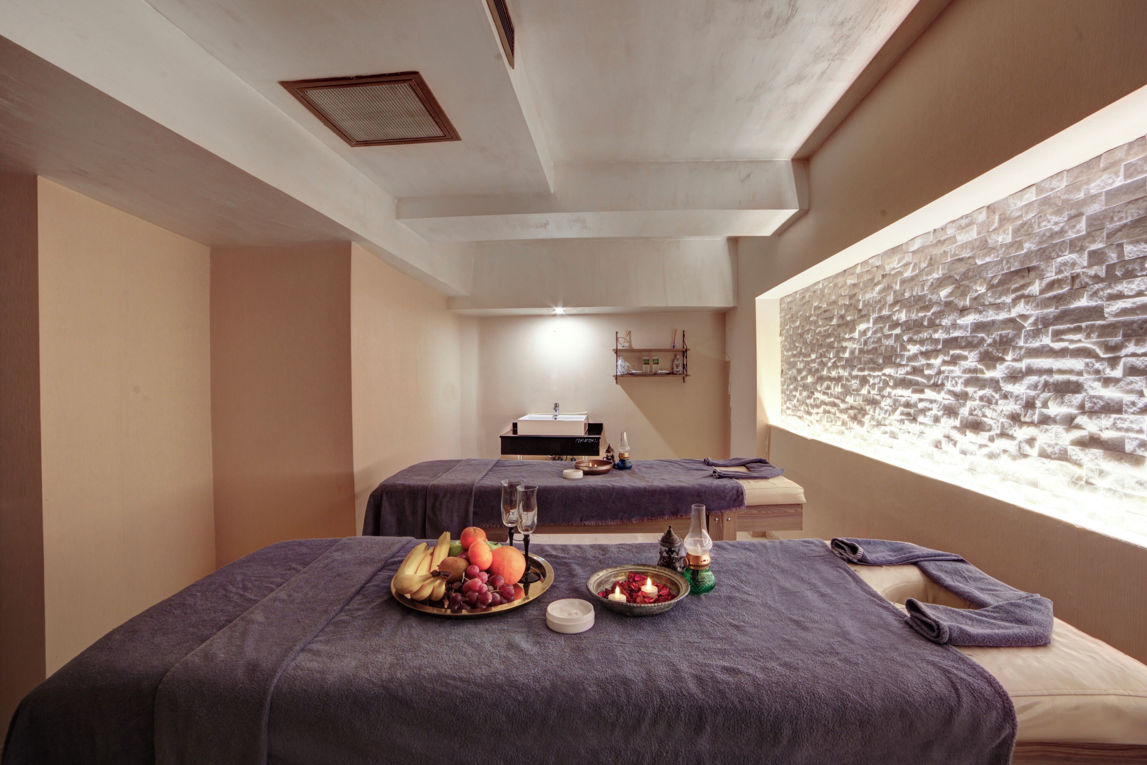 Quarto de spa com duas camas, um prato de frutas, velas e uma parede com textura.