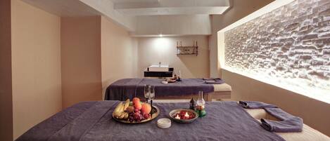 Quarto de spa com duas camas, um prato de frutas, velas e uma parede com textura.