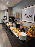 Um buffet com diversos tipos de comida, um relógio e um quadro com pássaros na parede.