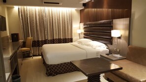 Quarto de hotel com uma cama, mesas de cabeceira, uma cadeira, escrivaninha e uma luminária.