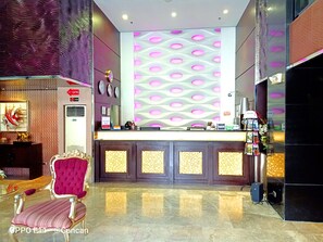 Uma área de recepção de hotel com design moderno, apresentando um balcão de atendimento, um relógio e uma placa indicando um spa.