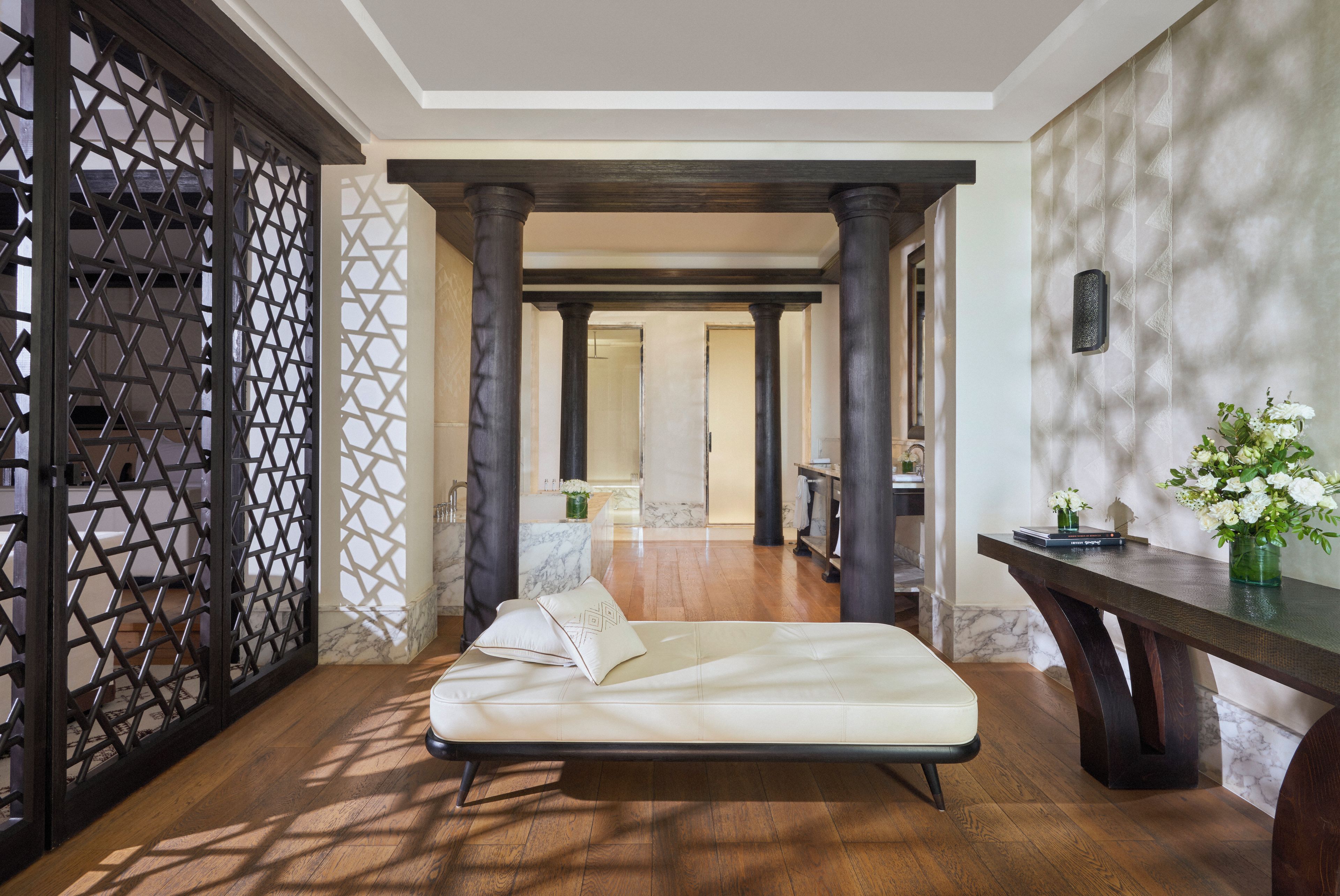 Quarto de hotel com sofá, piso de madeira, parede decorativa e vista para o corredor.