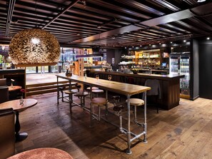 Uma área de bar com banquetas, balcão de madeira e luminária pendente.