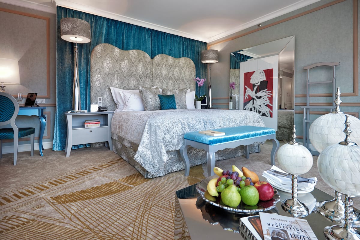 Quarto de hotel moderno com uma cama grande, uma escrivaninha, uma cadeira e uma mesa de jantar com frutas e uma revista.
