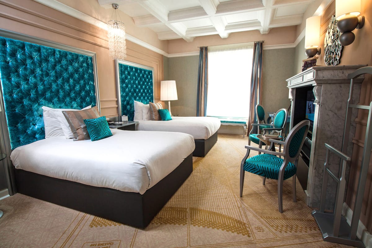 Quarto de hotel com duas camas, área de estar com cadeiras, uma escrivaninha e lareira.