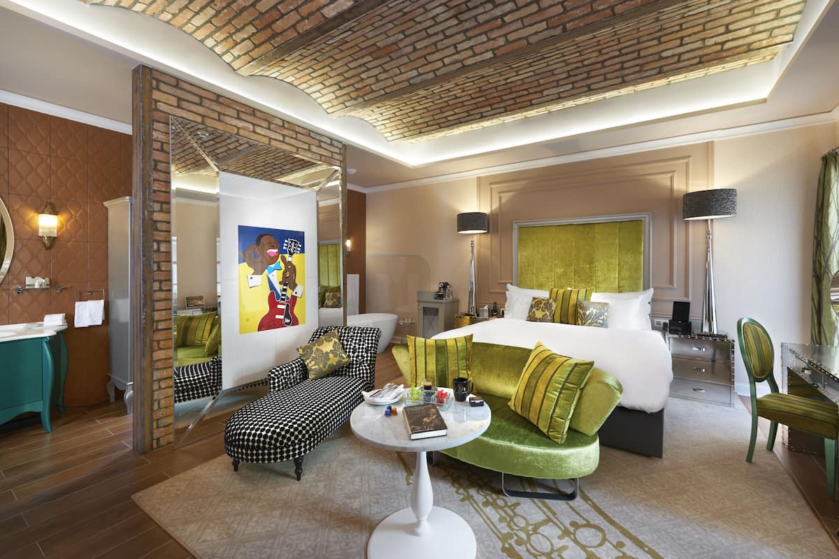 Quarto de hotel com uma cama grande, um sofá, uma mesa de jantar e um banheiro com espelho e pia.