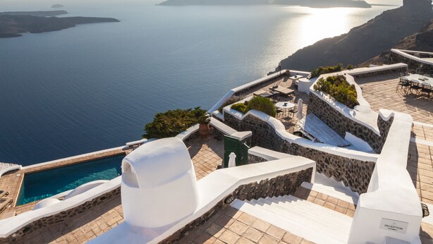 Um hotel à beira-mar com piscina, paredes de pedra e vista para o mar.