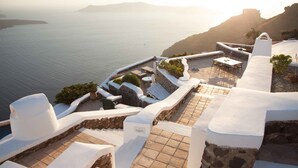 Terraço banhado por luz solar, com degraus de pedra e paredes brancas, com vista para um corpo d'água.