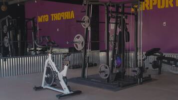 Academia com parede roxa, equipamentos de musculação e uma bicicleta ergométrica.