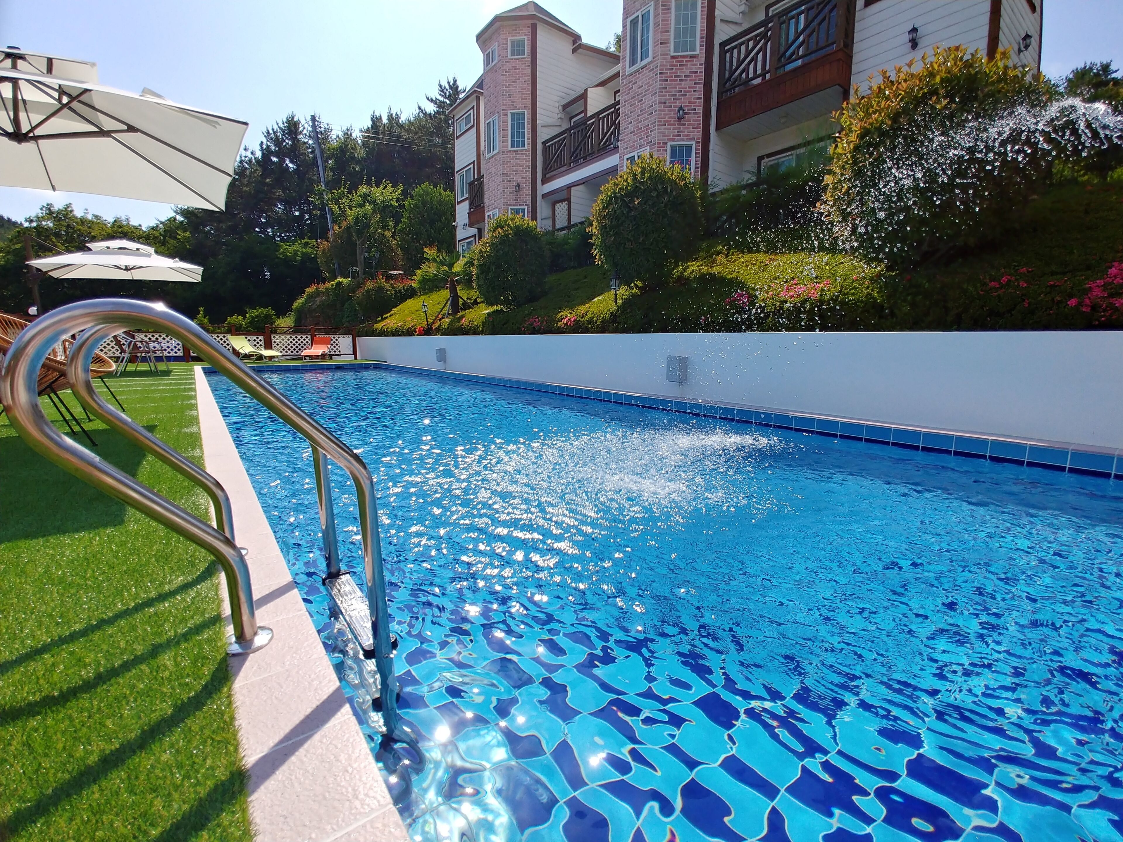 Piscina com escada de metal, cercada por um gramado bem cuidado e um edifício com varandas.